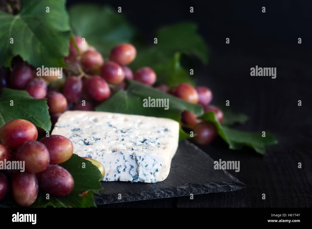 Blue cheese Dorblu with red grape on black background Stock Photo - Alamy