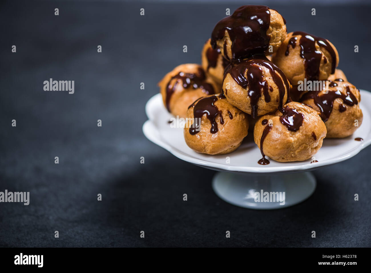 Stack of profiteroles eclairs with dark melted chocolate on platter ...