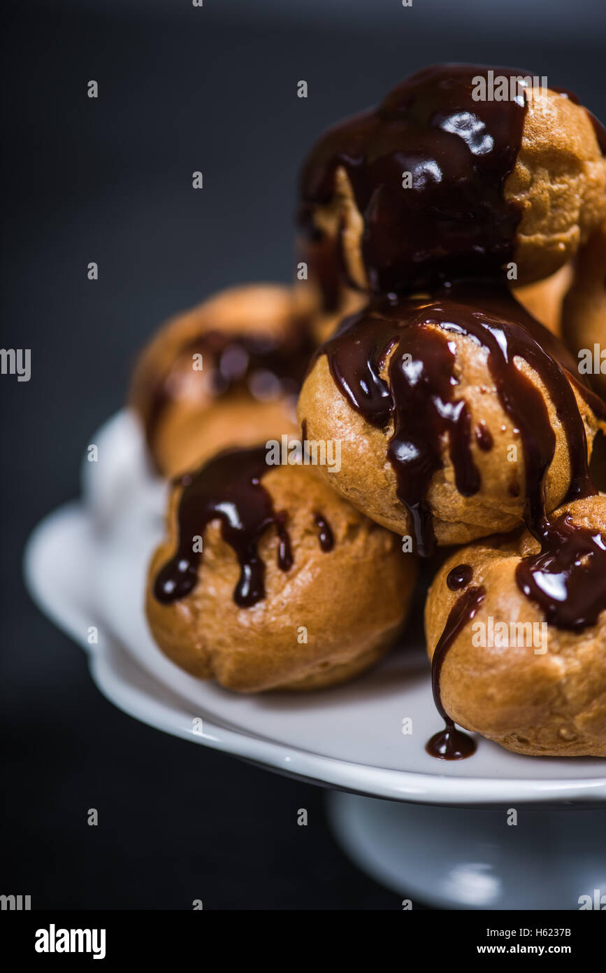 Stack of profiteroles eclairs with dark melted chocolate on platter ...