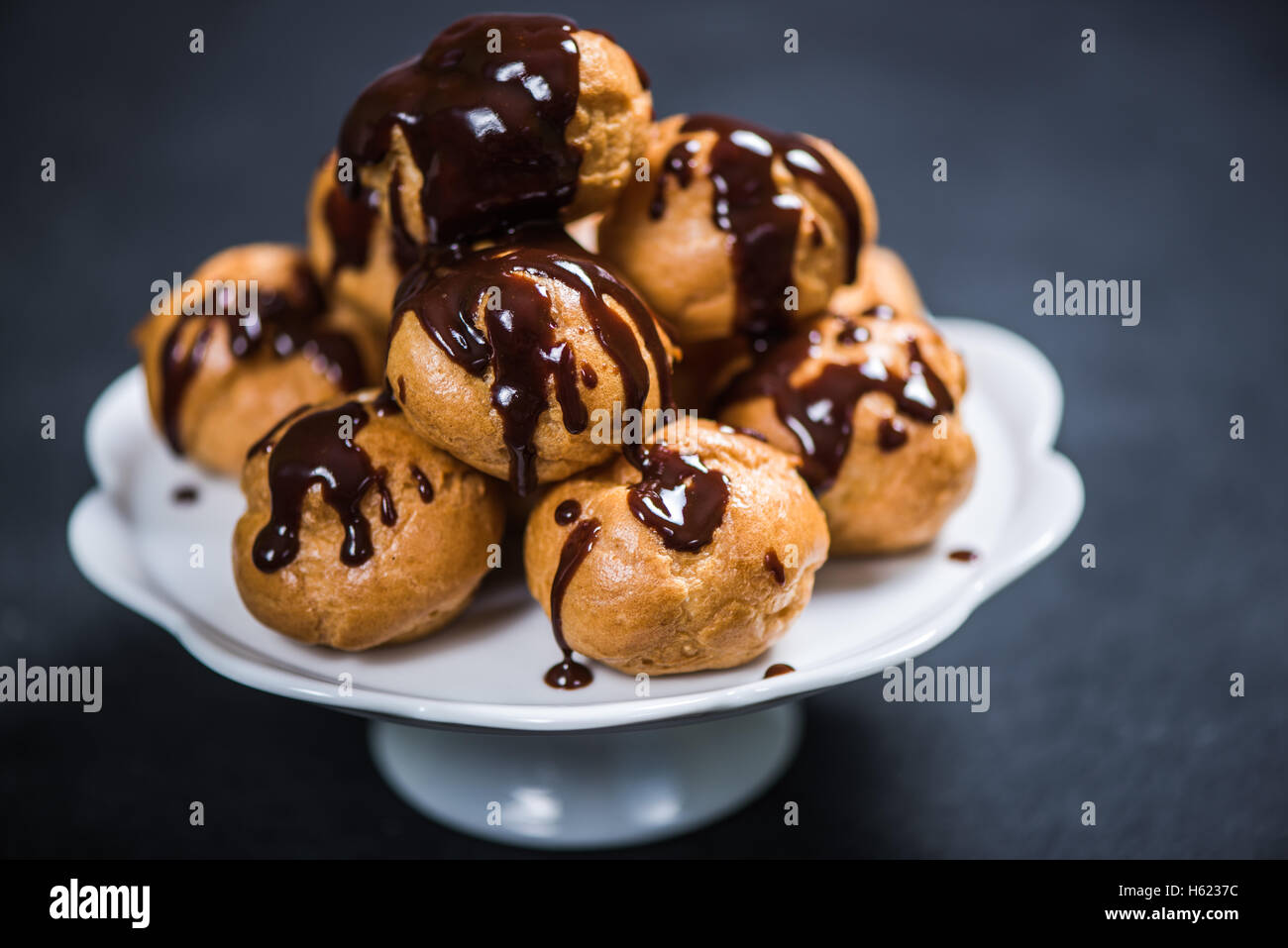 Stack of profiteroles eclairs with dark melted chocolate on platter ...