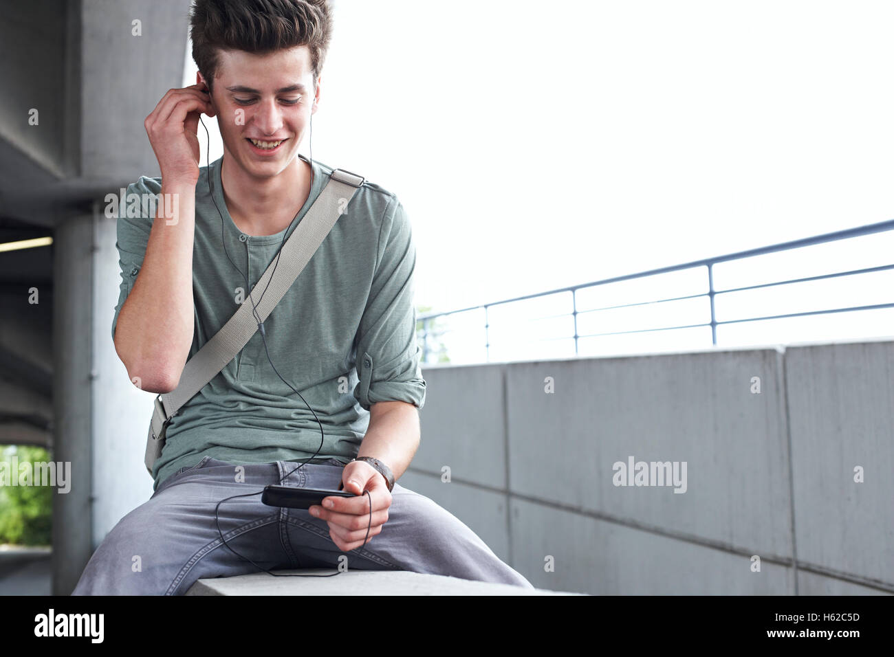 Smiling teenage boy with cell phone and earbuds outdoors Stock Photo ...
