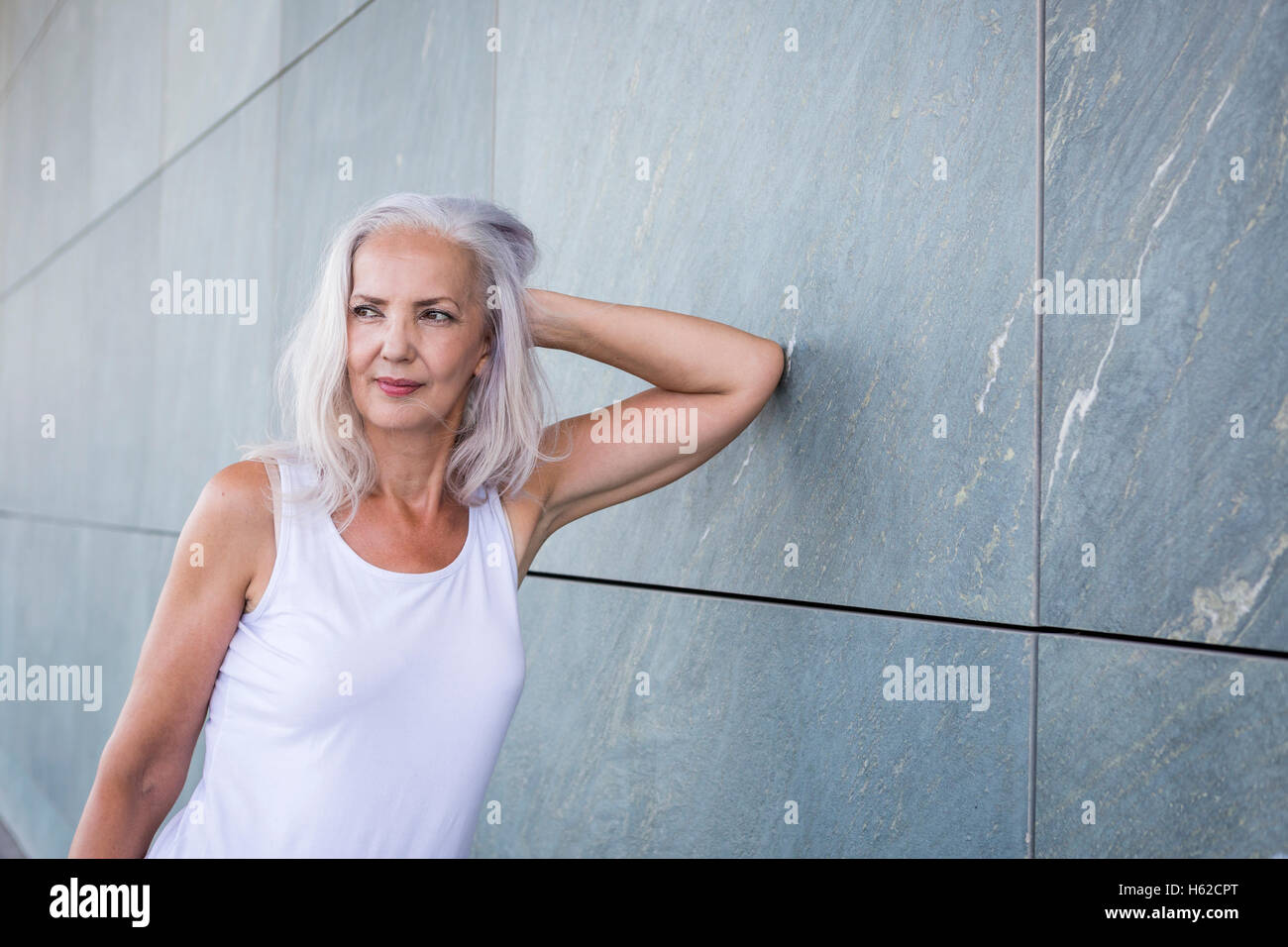 Portrait of woman leaning against wall watching something Stock Photo ...