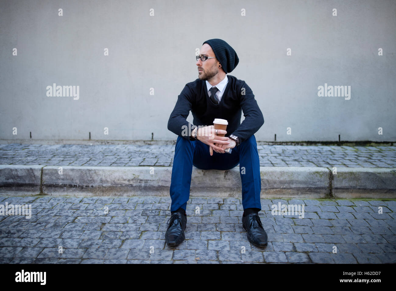Young man sitting on curb with takeaway coffee Stock Photo - Alamy