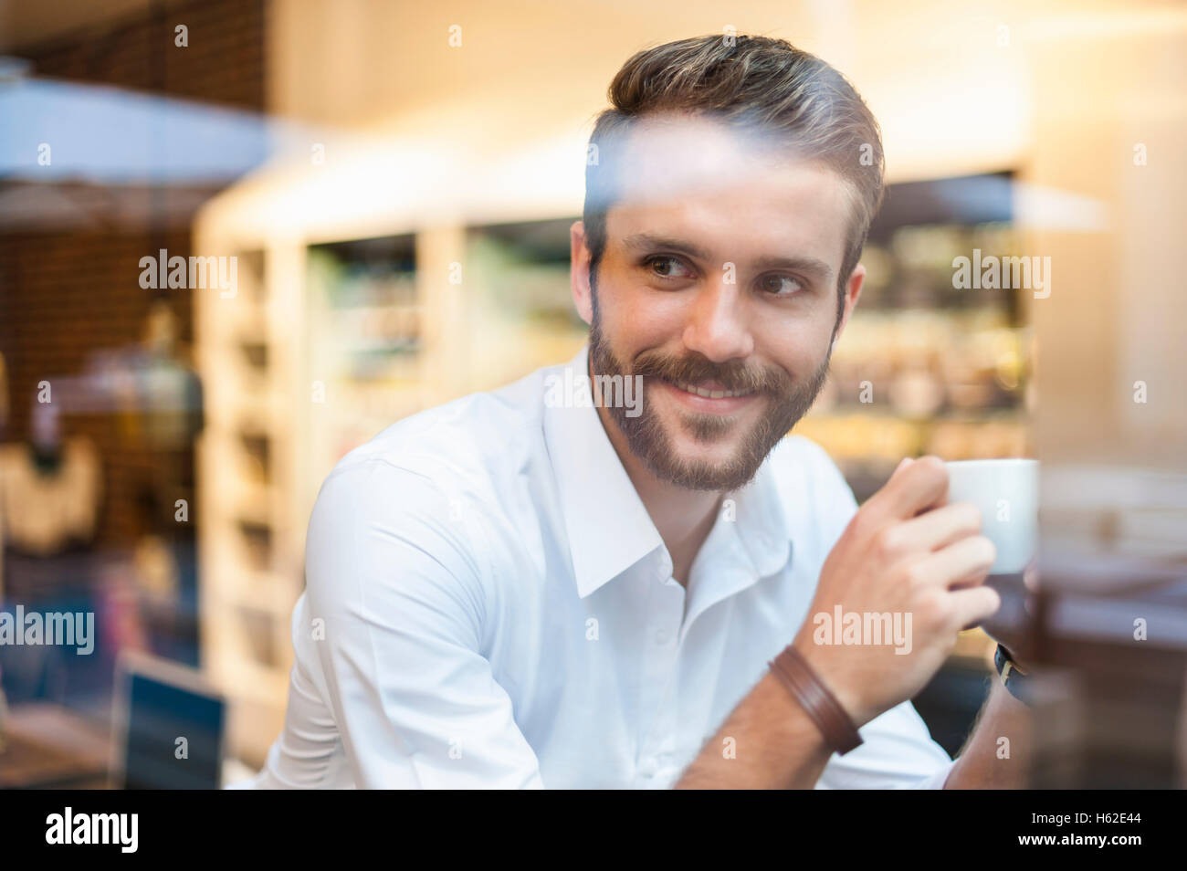 Smiling businessman holding cup of coffee behind windowpane in a cafe ...
