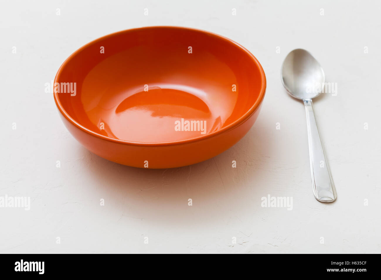 orange bowl and spoon on white plastering plate Stock Photo - Alamy