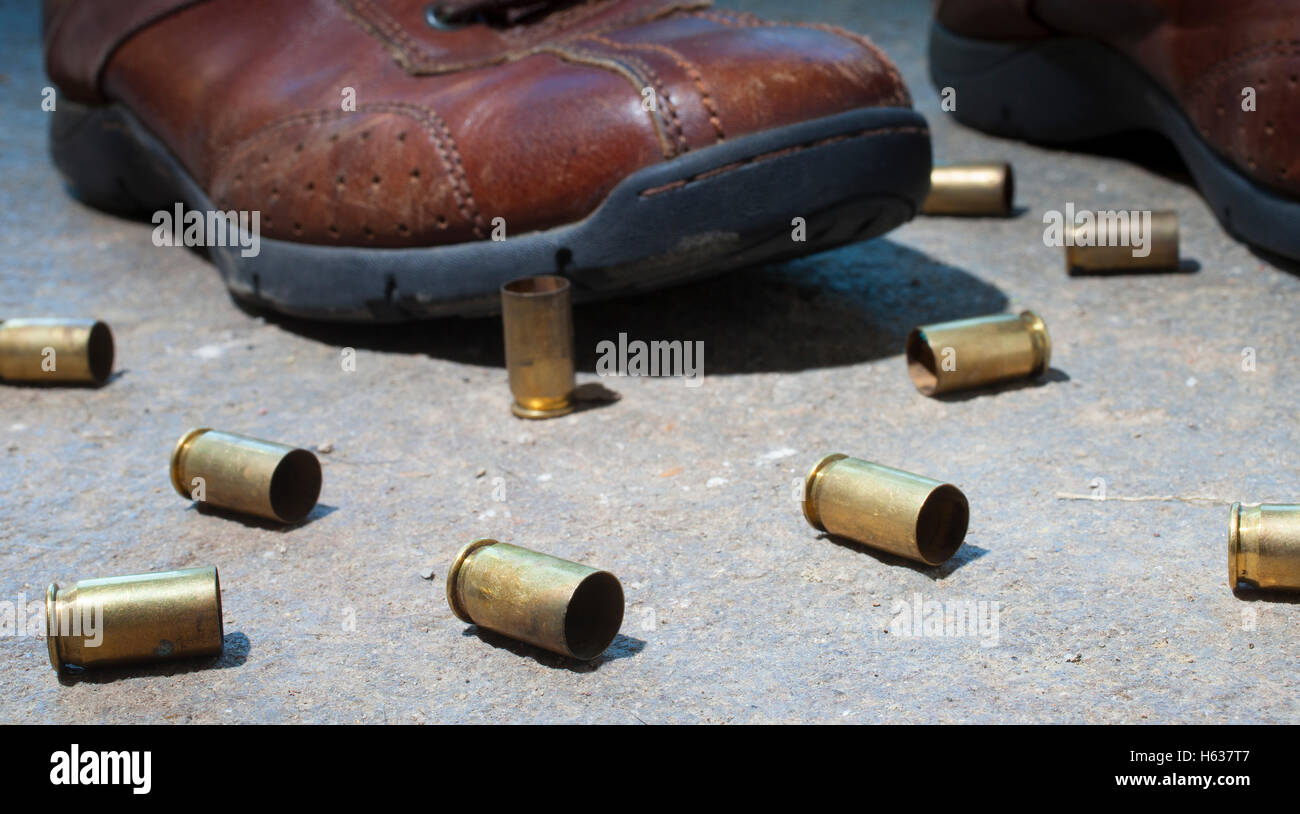 Brown shoes that are surrounded by empty handgun brass on concrete ...