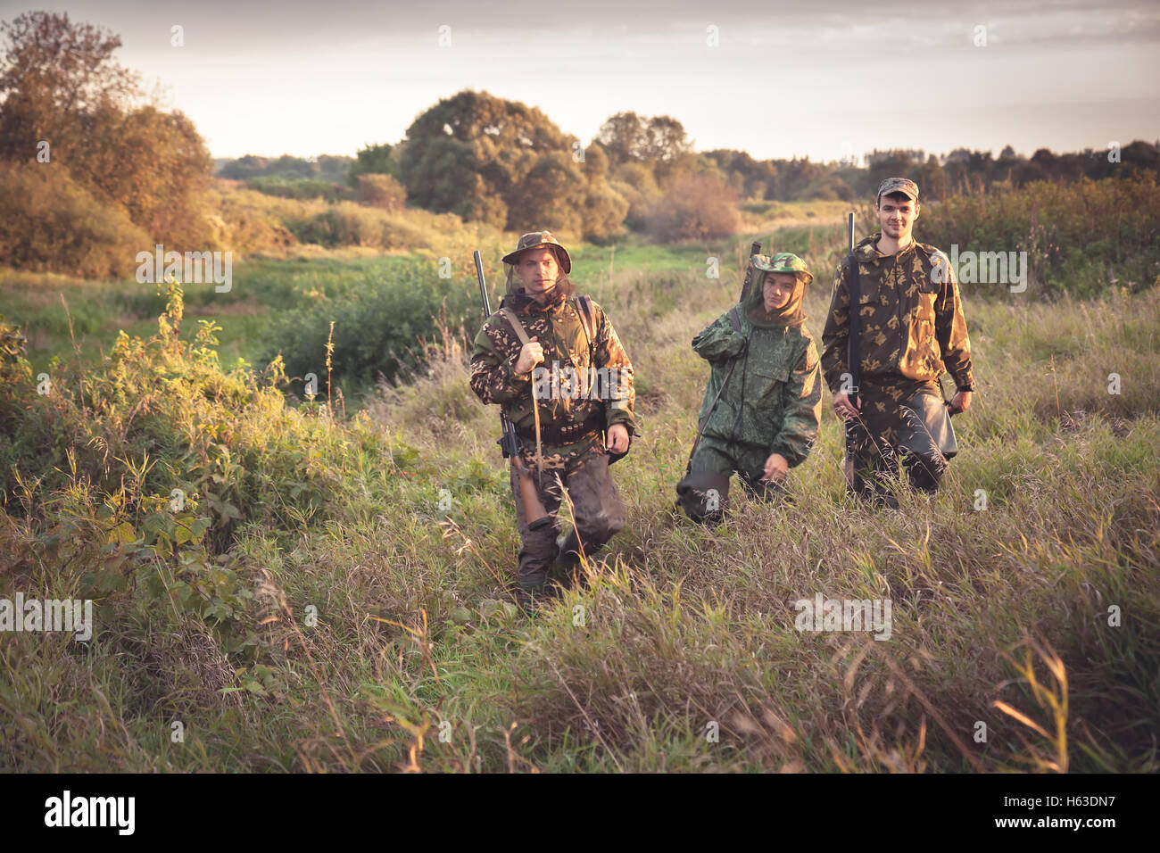 Hunters going through tall garass in rural field at dawn during hunting ...