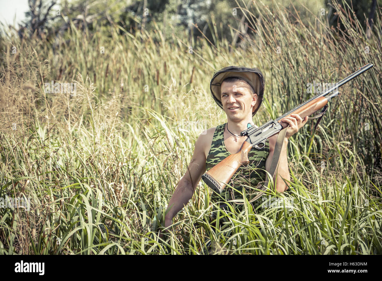 Hunter man in rural field with shotgun break through tall reed grass ...