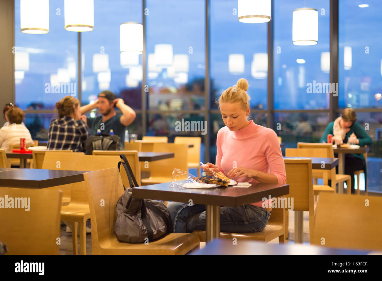 Young woman eating pizza at airport restaurant while waiting for flight ...