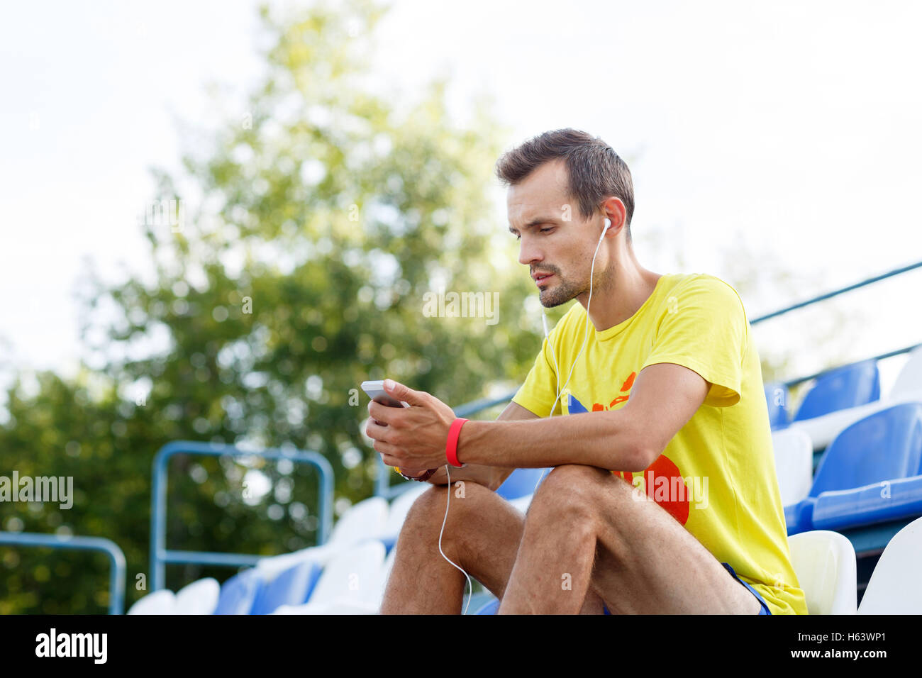 Young athlete looks into phone while listening music in summer at ...