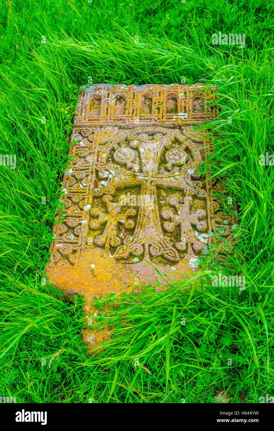 The old khachkar with the relief of cross, lays in tall grass of ...