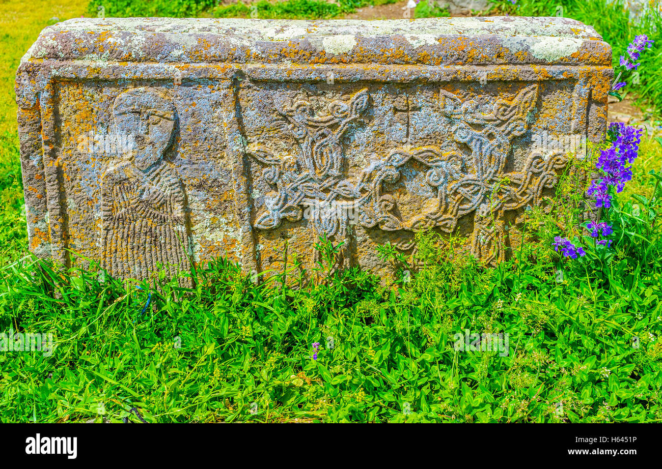 The old khachkar with carved crosses and praying monk, surrounded with ...