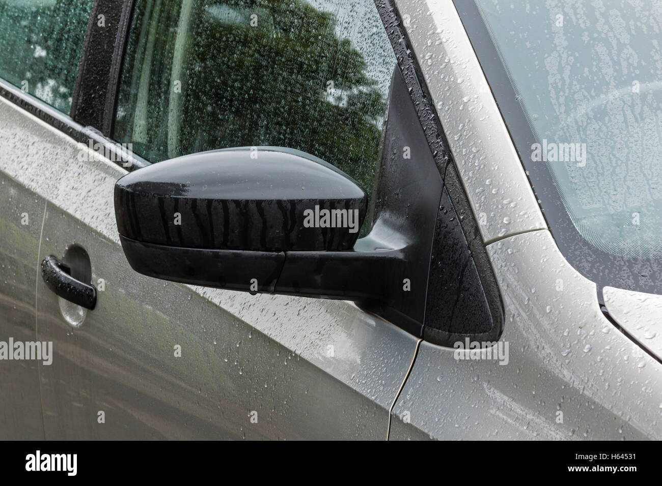 Close up front side view of motor vehicle door windows and rear view mirror covered in rain ...