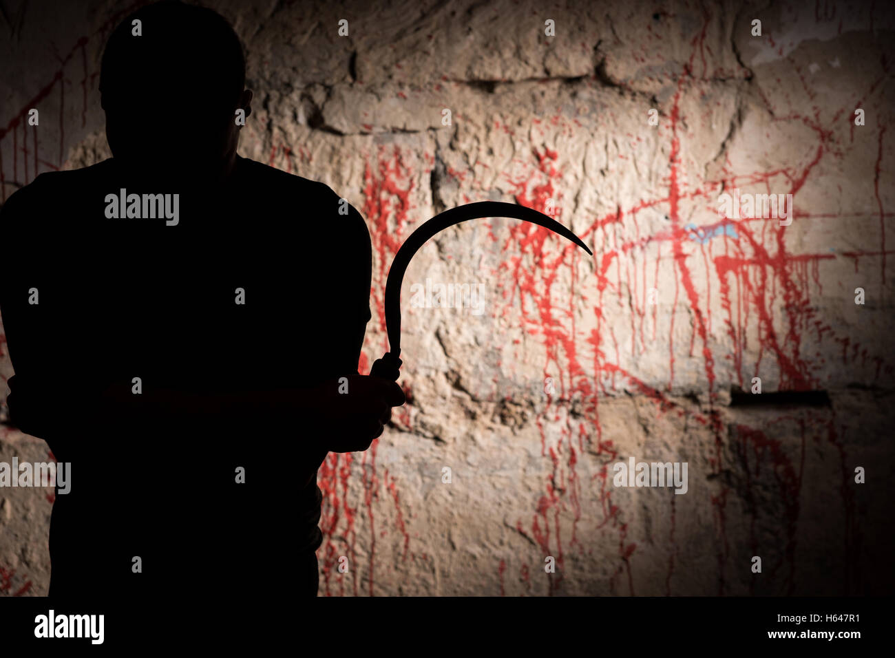 Portrait of shadowy figure holding blade near blood stained wall for ...