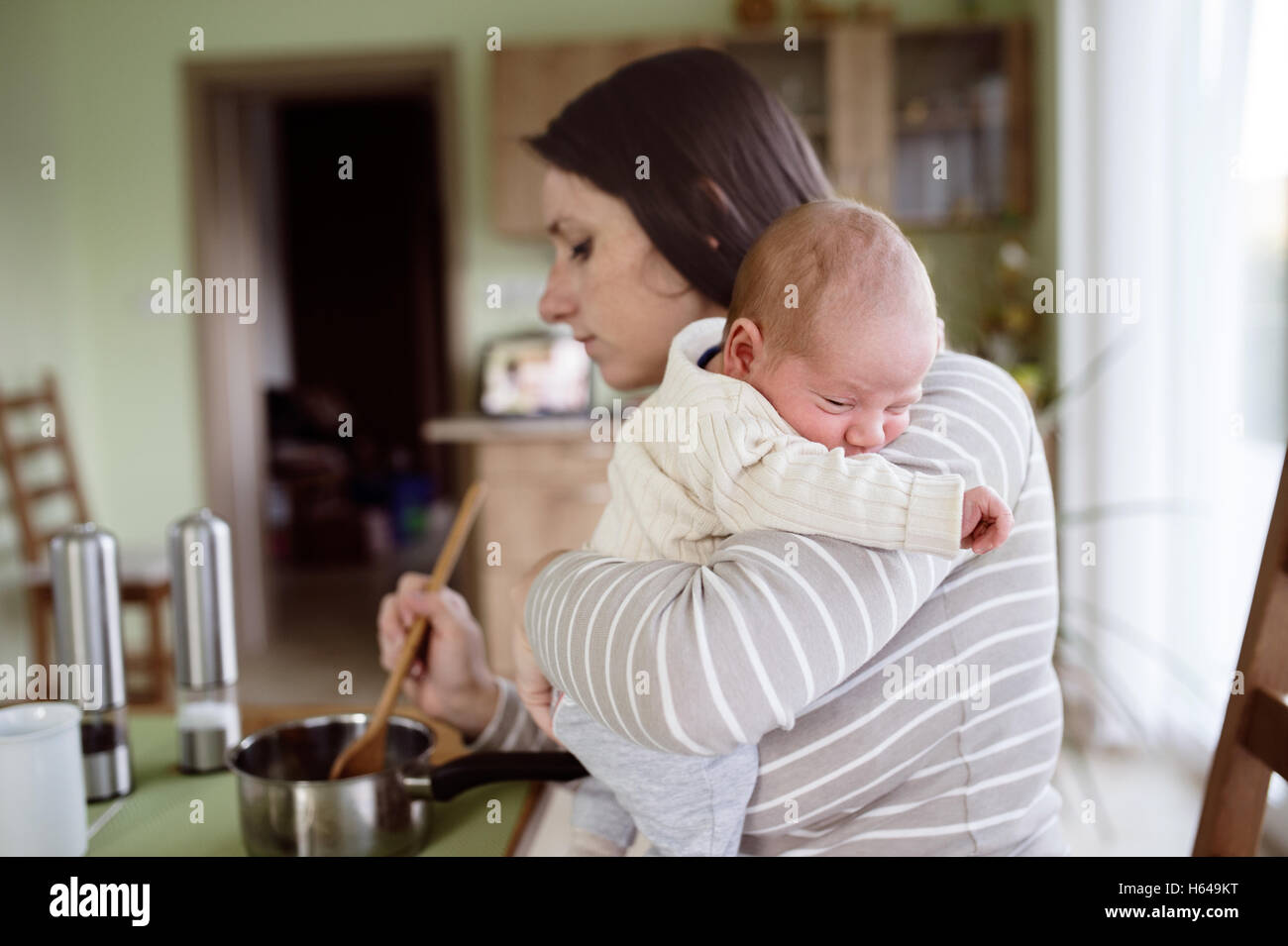 Young mother in kitchen holding baby son, cooking Stock Photo - Alamy