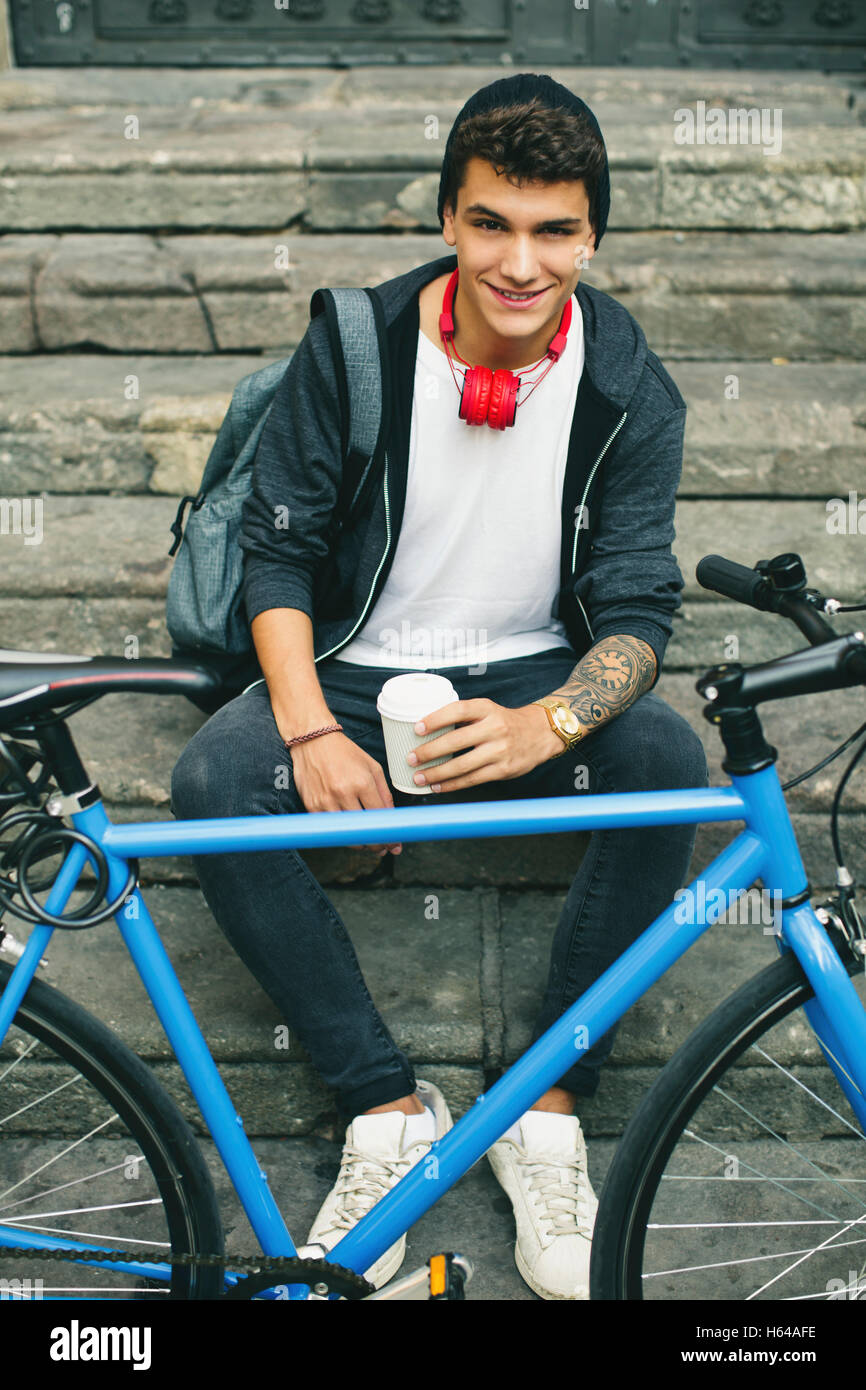 Teenager with a fixie bike sitting on steps, coffee to go, smiling ...
