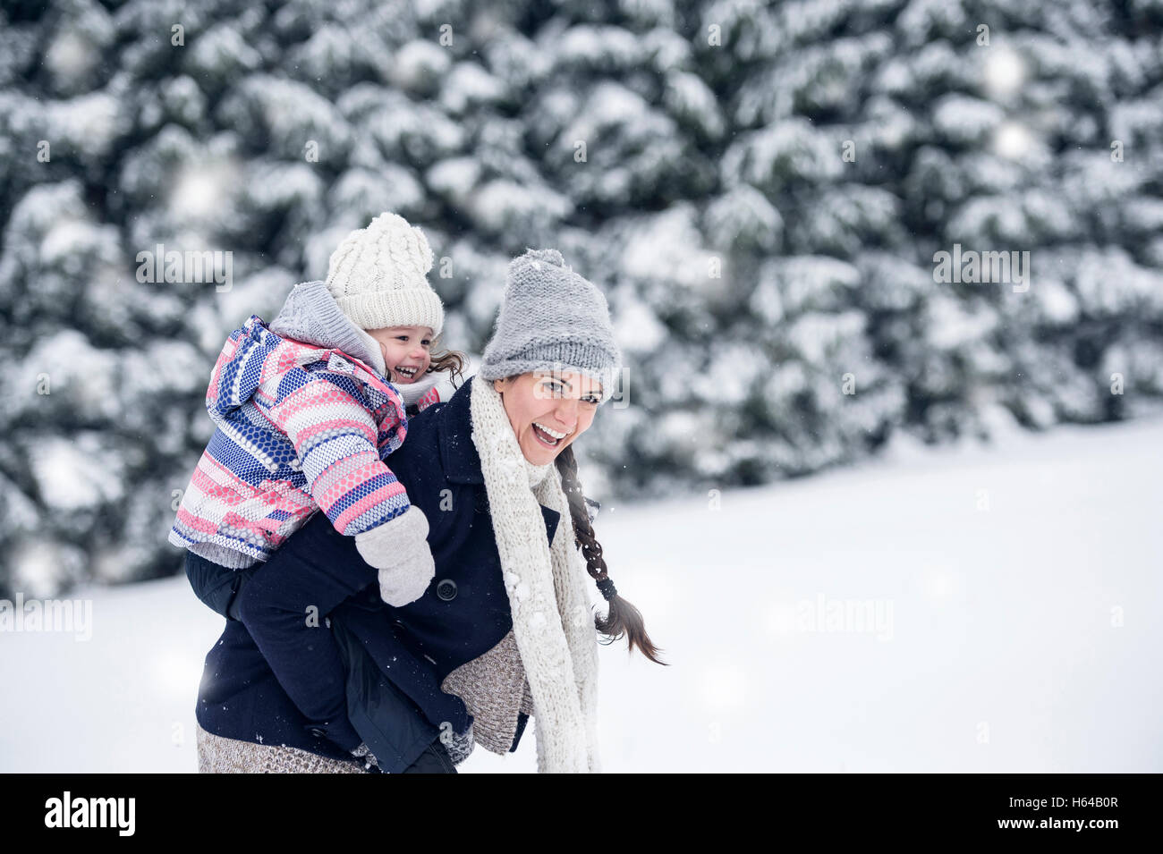 Happy mother carrying daughter piggyback in winter landscape Stock ...