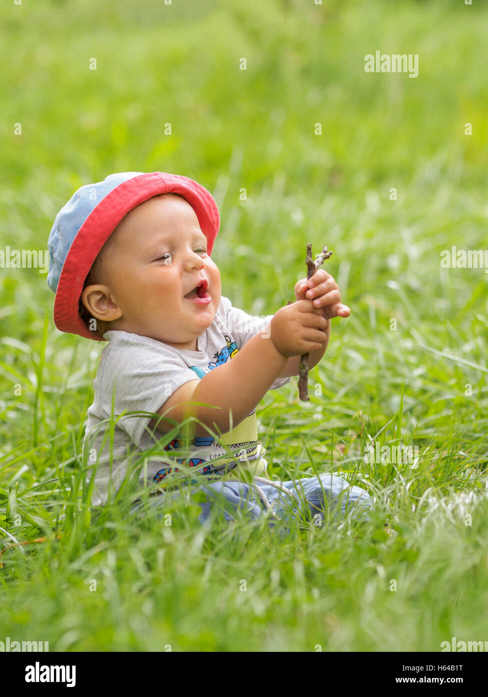 Happy baby boy sitting on a meadow playing with twig Stock Photo - Alamy
