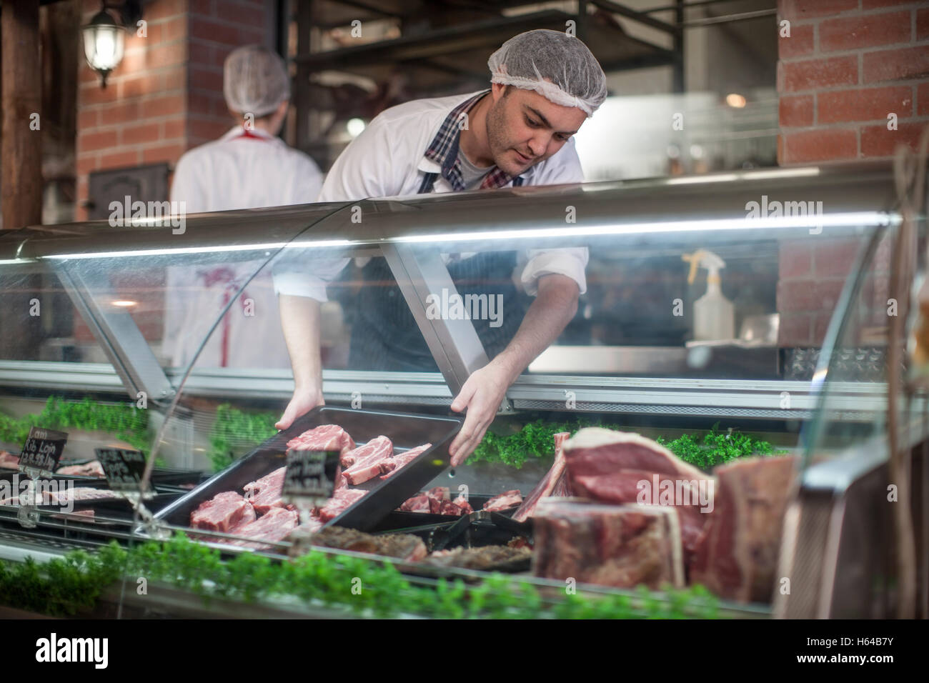 Butcher putting fresh meat on display in butchery Stock Photo - Alamy