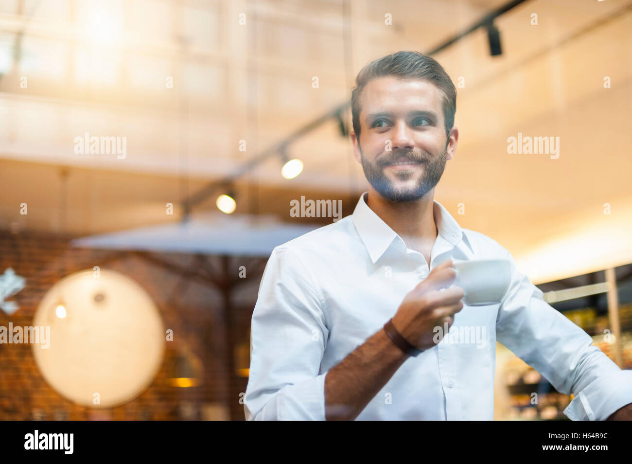 Smiling businessman holding cup of coffee behind windowpane in a cafe ...