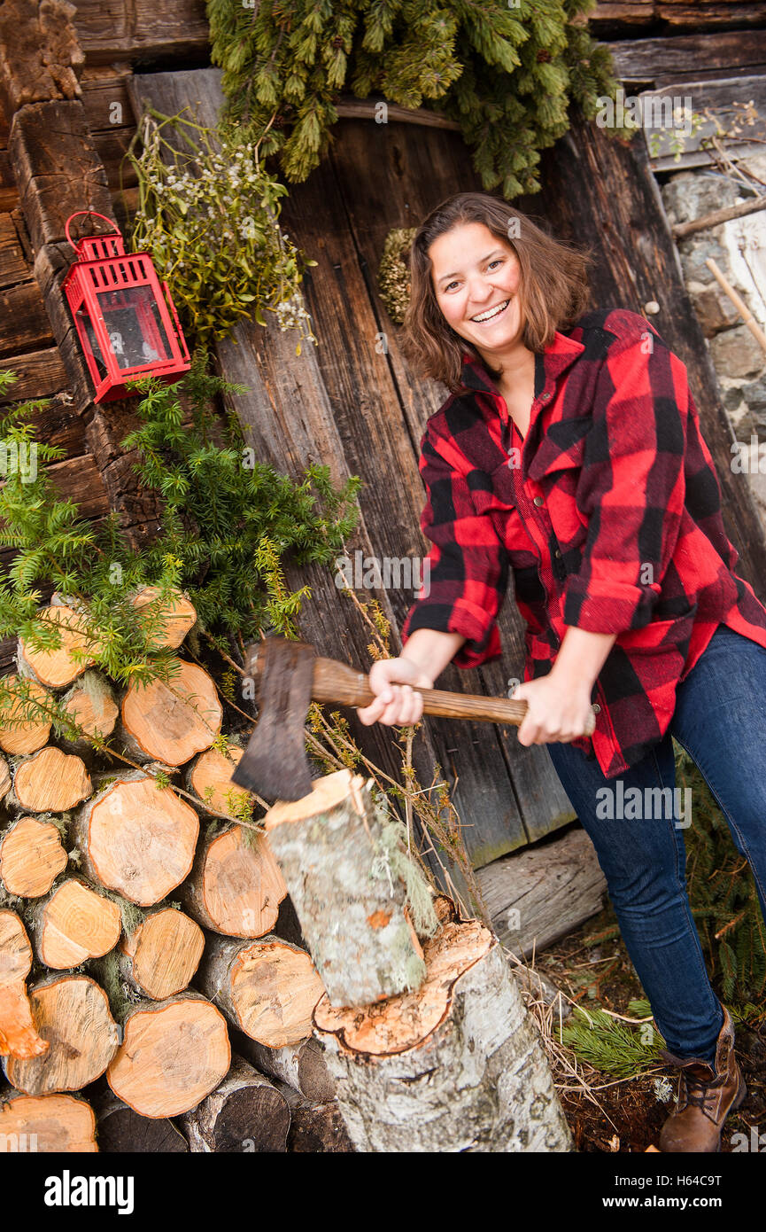 Smiling woman chopping wood in front of wooden hut Stock Photo - Alamy