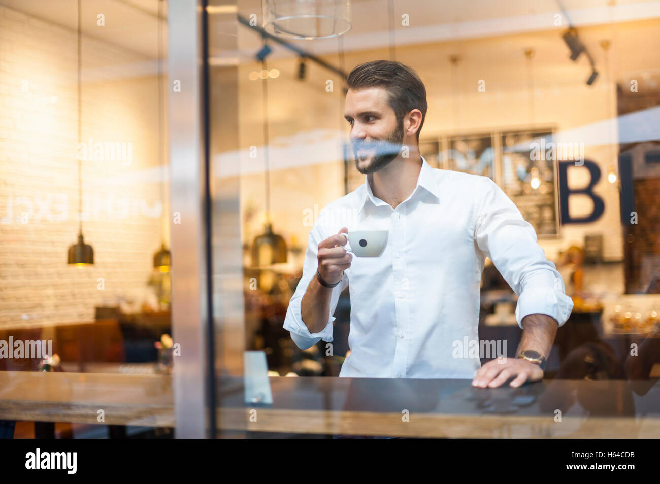Smiling businessman holding cup of coffee behind windowpane in a cafe ...