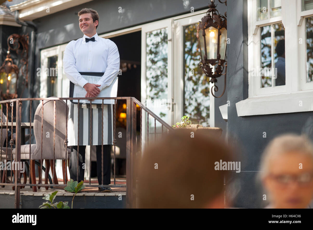 Waiter on porch looking around at outdoor restaraunt Stock Photo - Alamy