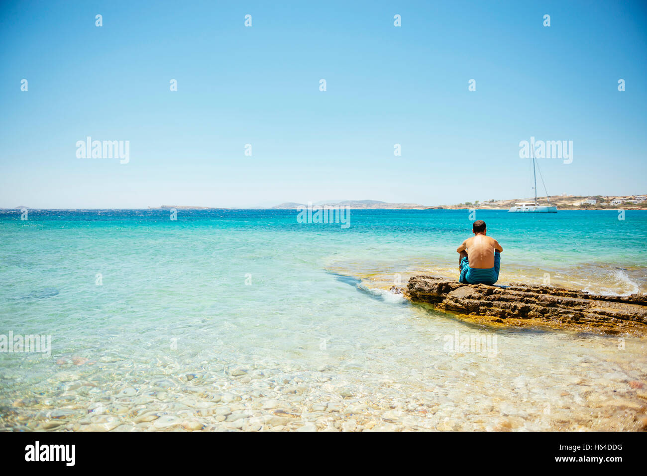Greece, Koufonissi, Man sitting on rock looking at clear water of the ...