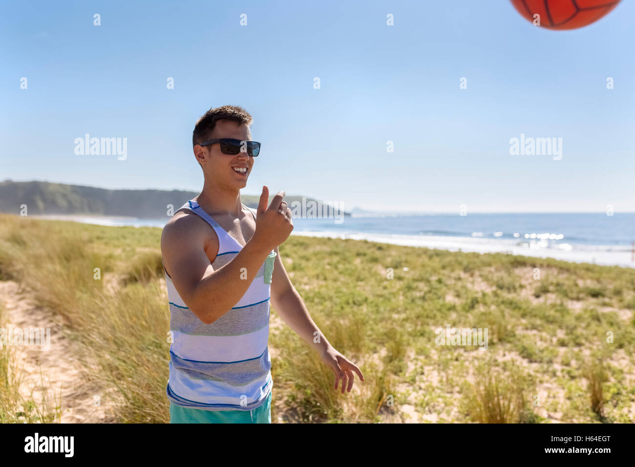 Smiling young man playing with ball on the beach Stock Photo - Alamy