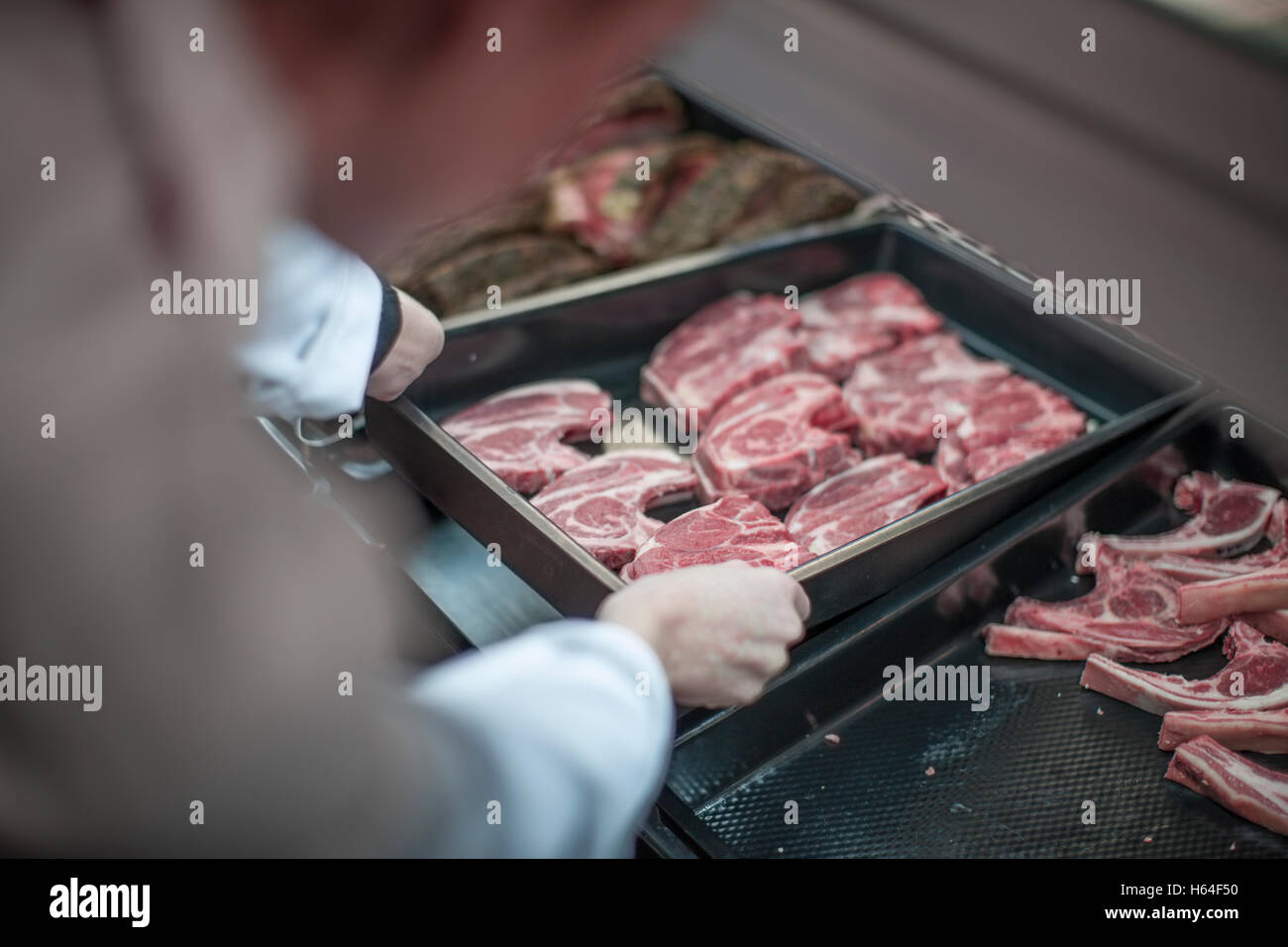 Butcher putting fresh meat on display in butchery Stock Photo - Alamy