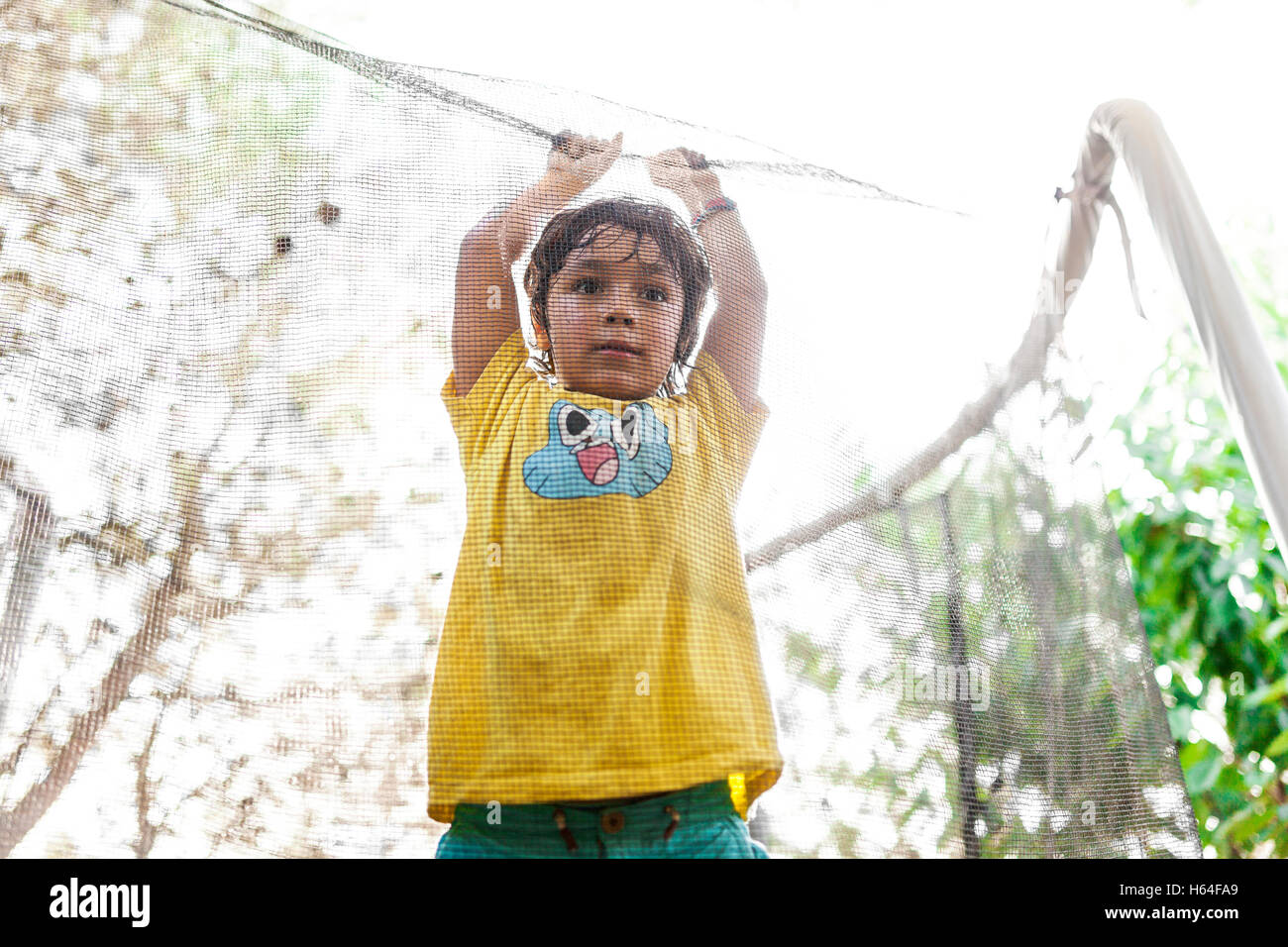 Little boy standing behind net of trampoline Stock Photo - Alamy