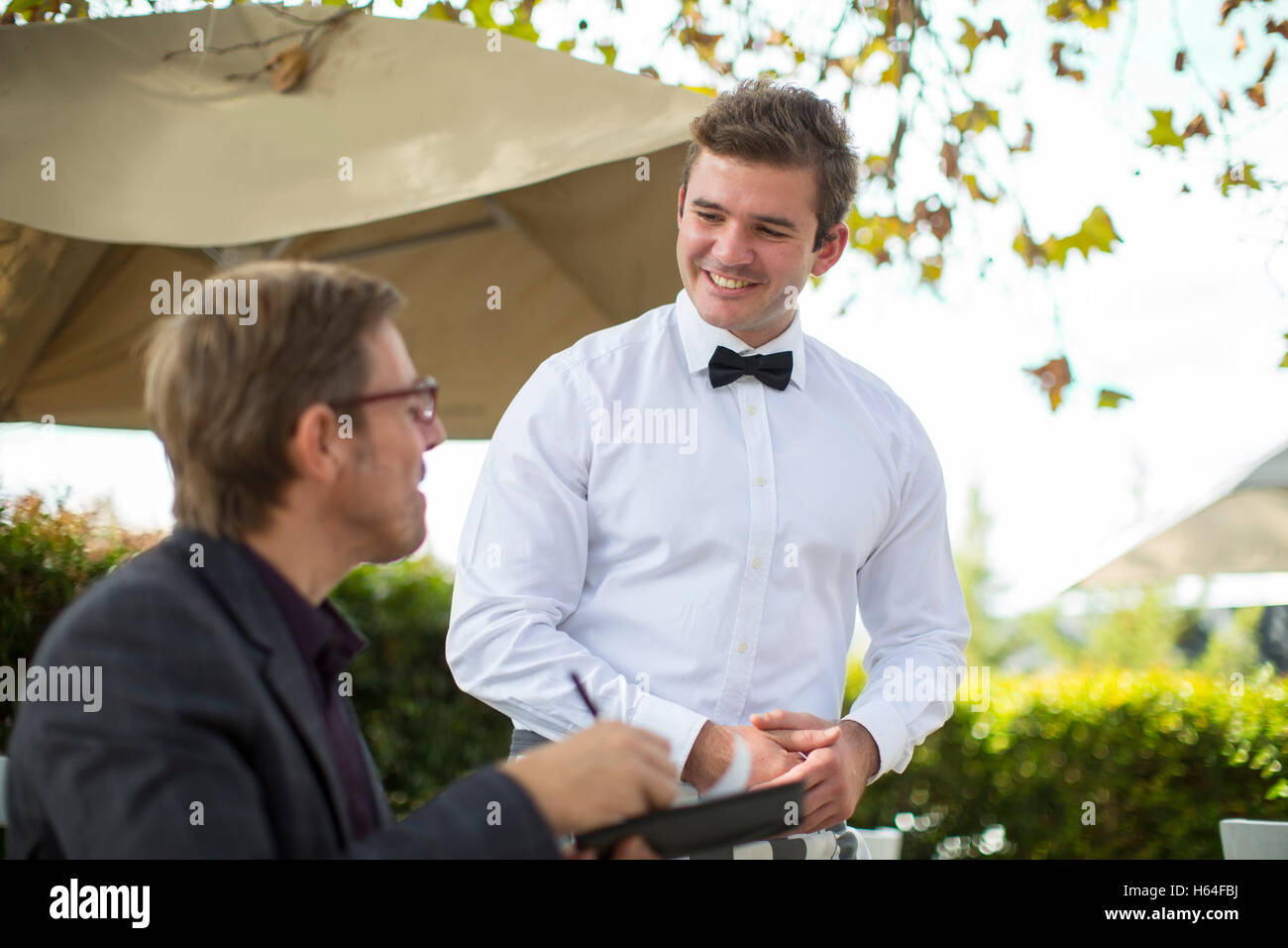 Waiter smiling at businessman at outdoor restaraunt Stock Photo - Alamy