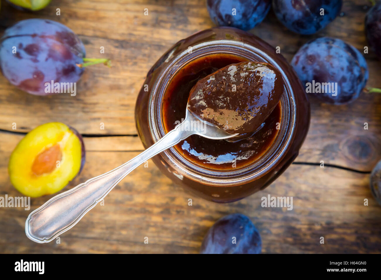 Tea spoon of plum jam on preserving jar and plums on wood Stock Photo ...