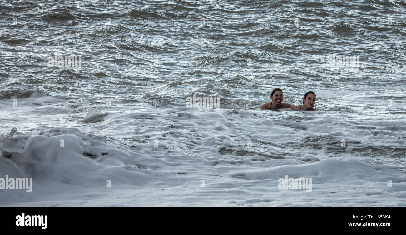 Two young women swimming in a very cold and storm sea with waves and ...