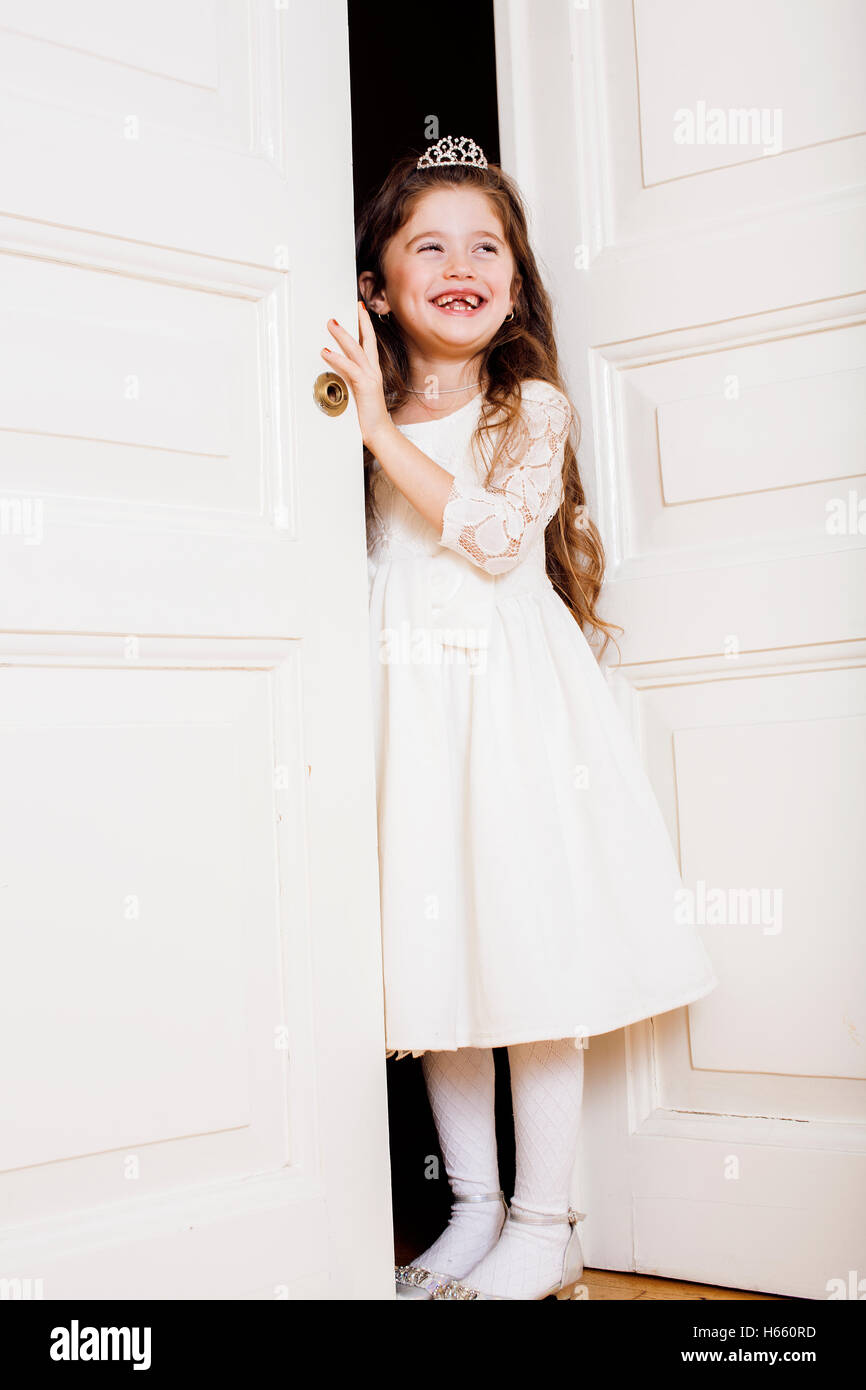 little cute girl at home, opening door well-dressed in white dress ...