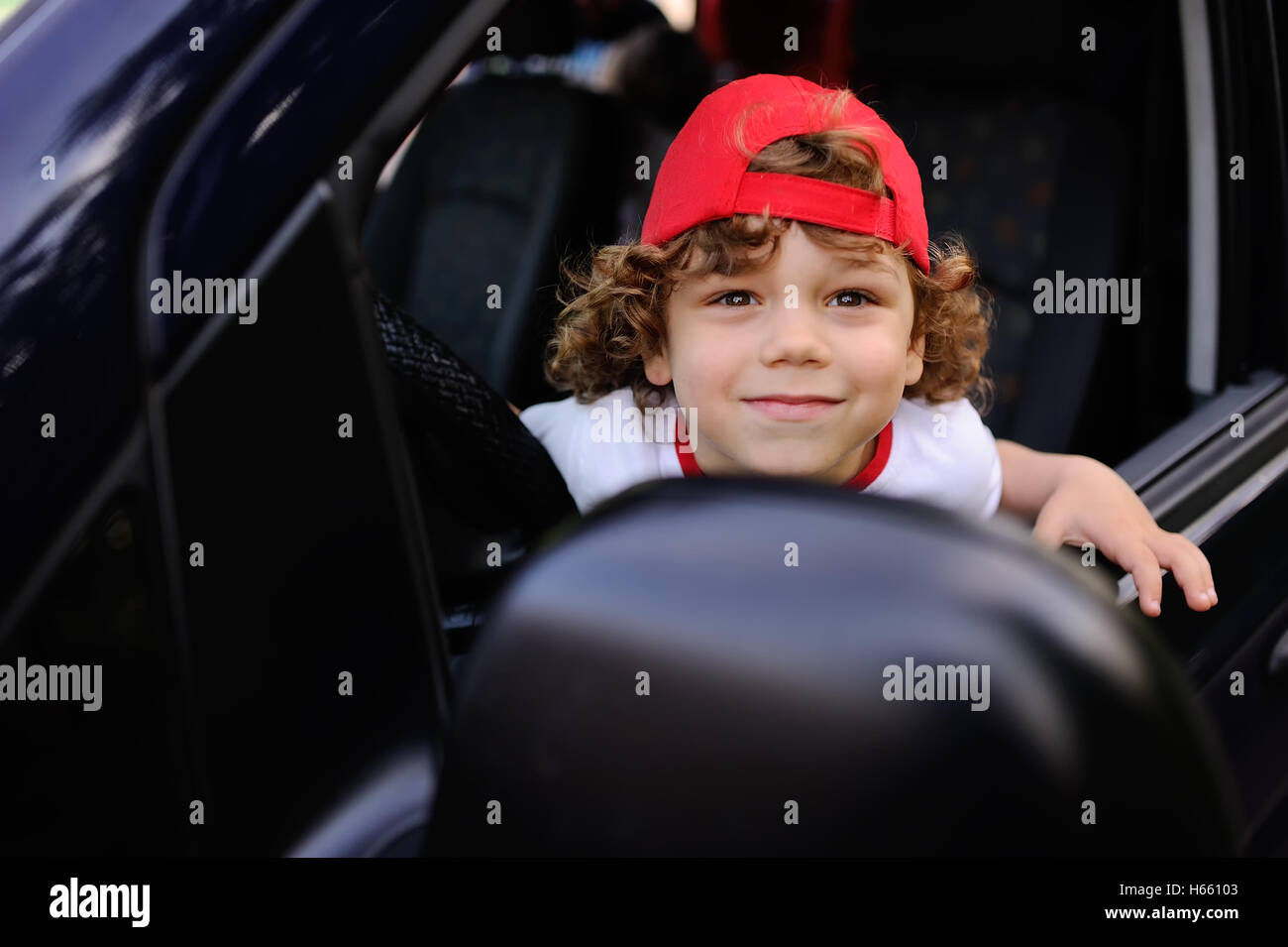 child with curly hair and a red cap sits behind the wheel of car Stock ...