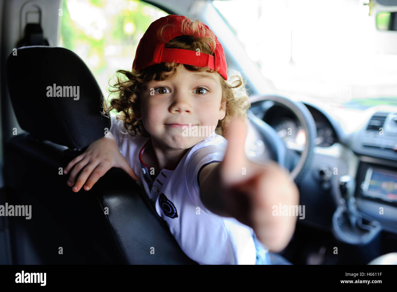 child with curly hair and a red cap sits behind the wheel of car Stock ...