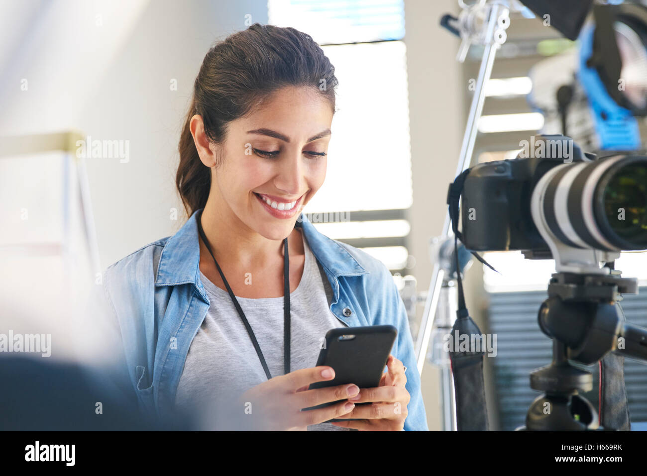 Smiling female photographer using cell phone behind camera in studio ...