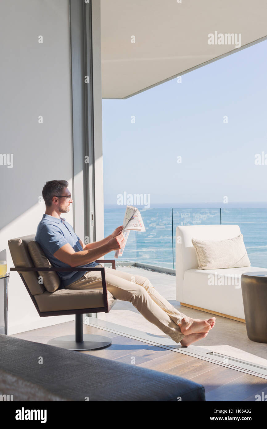 Man relaxing reading newspaper in sunny patio doorway with ocean view ...