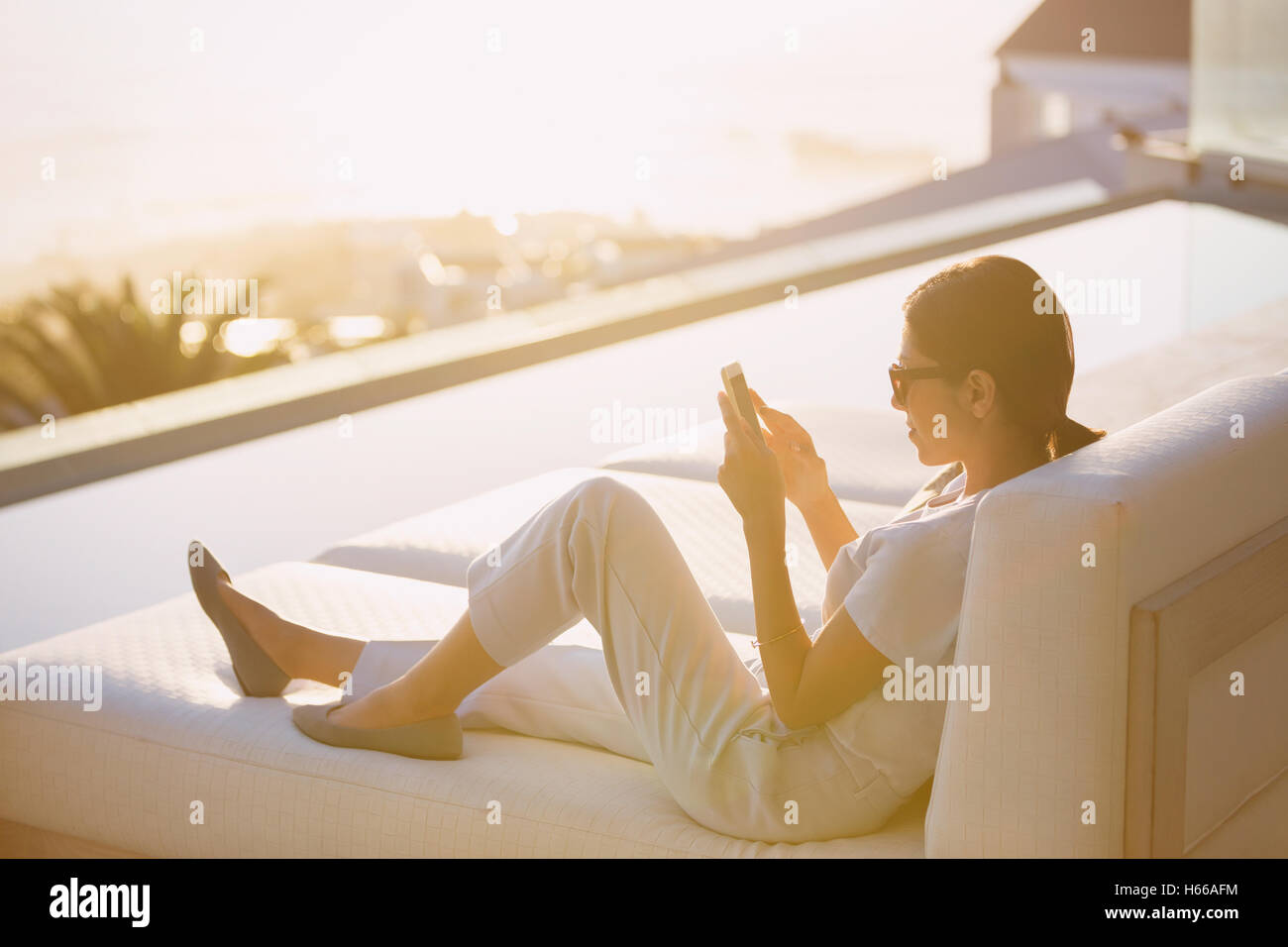 Woman using cell phone on chaise lounge at poolside on luxury patio ...