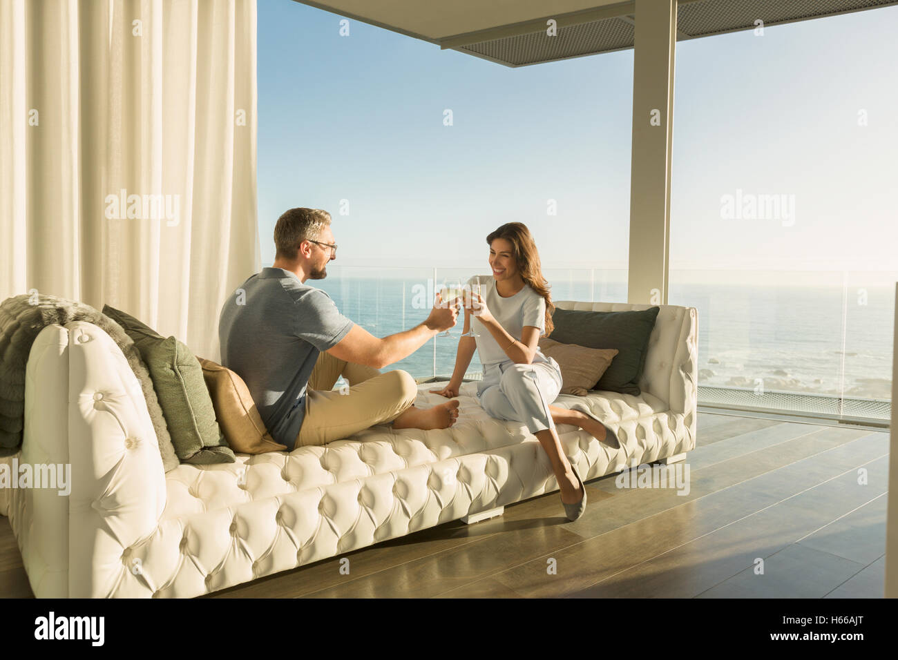 Couple toasting wine glasses on luxury tufted chaise lounge with ocean ...