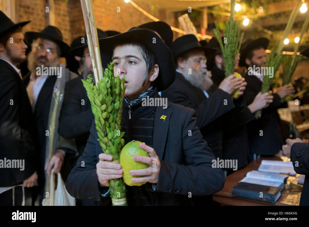A religious Jewish boy blessing an etrog & lulav in a crowded Sukah in ...