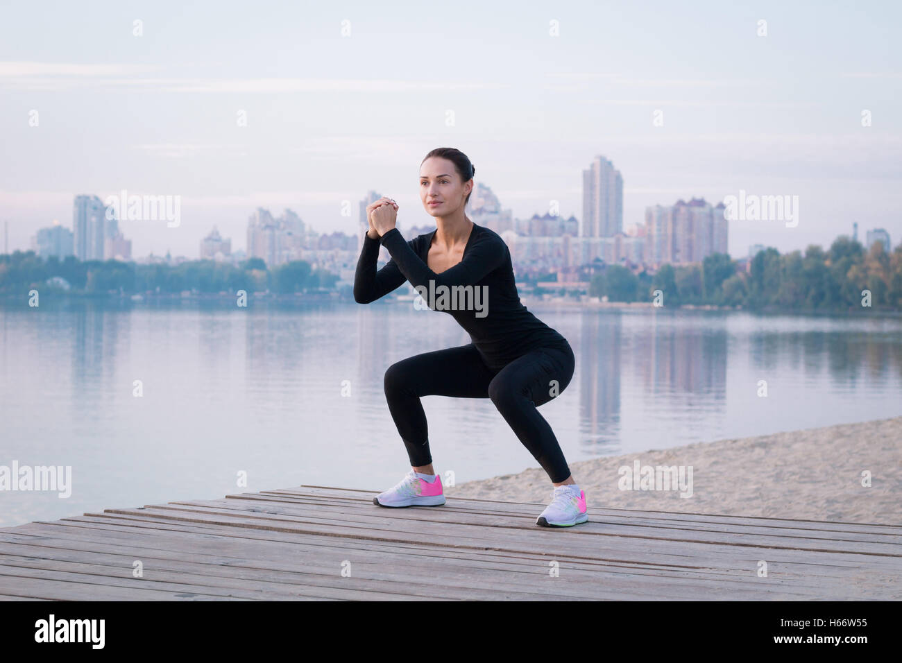 Young pretty fitness woman exercises on pier during morning training ...