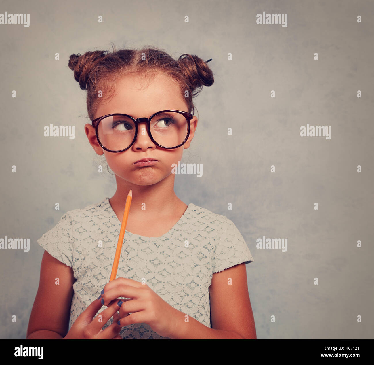 Thinking grimacing kid girl in glasses looking and holding pencil in ...
