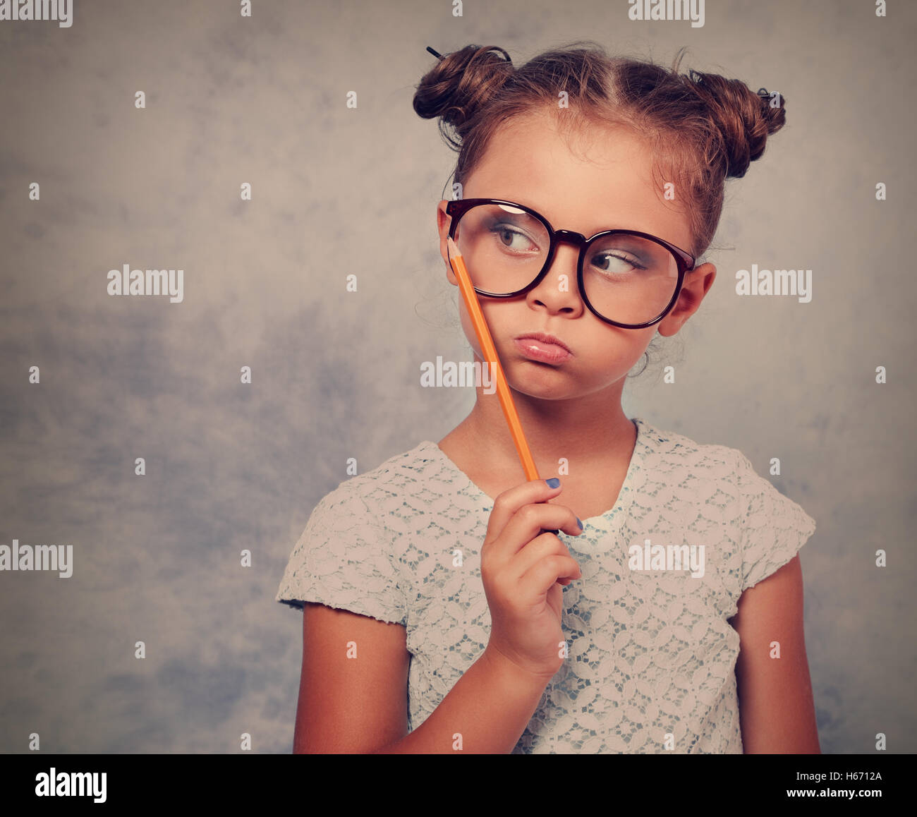 Thinking grimacing kid girl in glasses looking and holding pencil in ...
