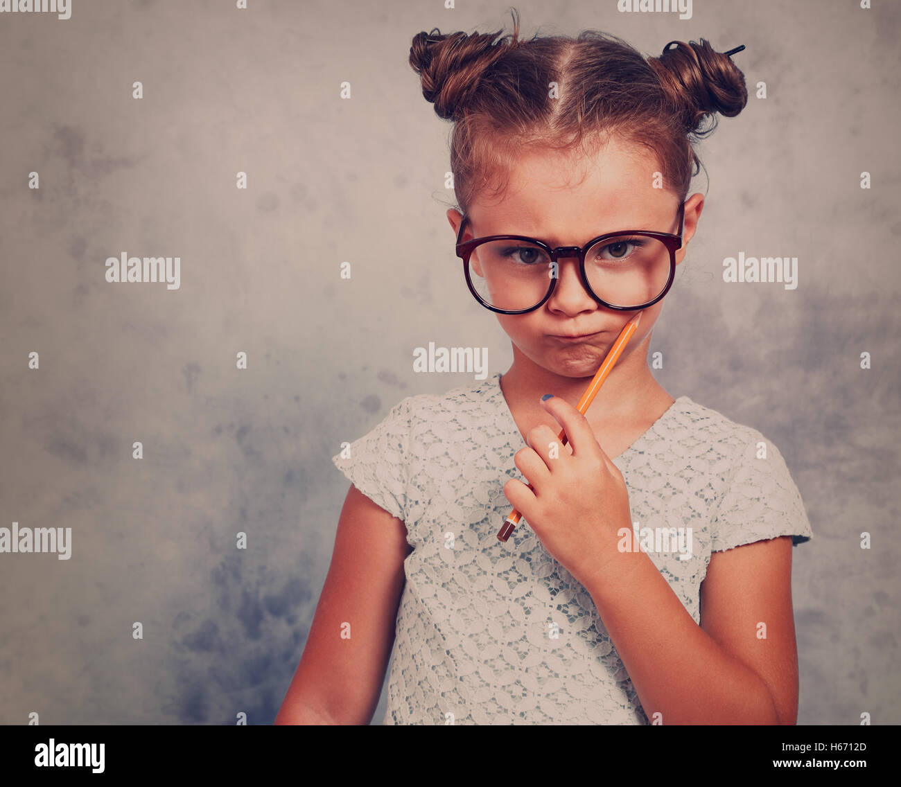 Serious strict kid girl in eye glasses holding pencil and thinking ...