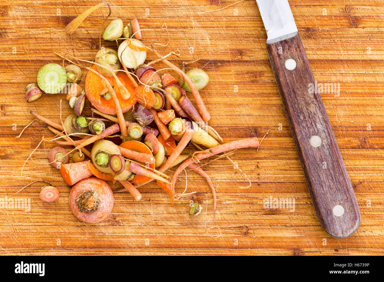 Scraps leftover from cutting raw carrots beside knife over large wooden ...