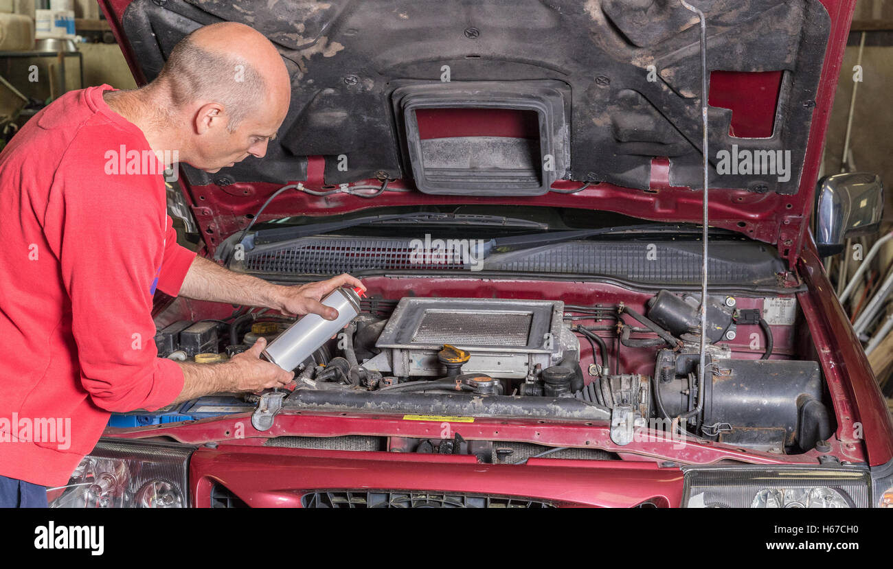 Mechanic working on a car engine he is holding a can or aerosol spray ...