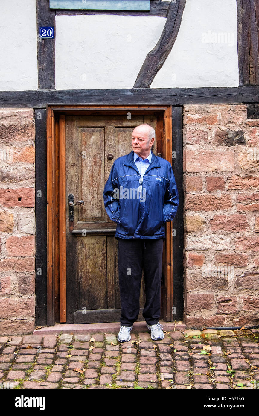 Elderly man stands outside building with small wooden door & timber ...