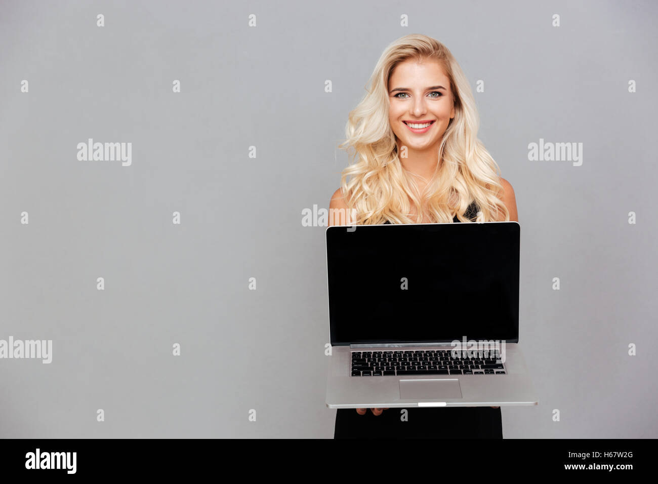 Smiling blonde woman with long hair showing blank laptop computer ...